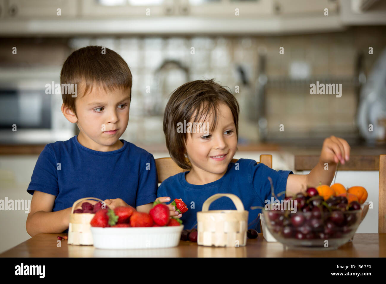 Two sweet children, boy brothers, eating fresh fruits at home ...