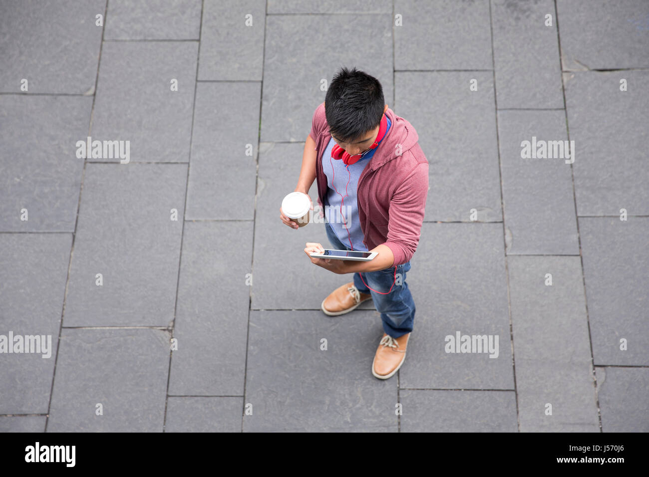 High angle view of a Chinese man standing on city street using a tablet ...