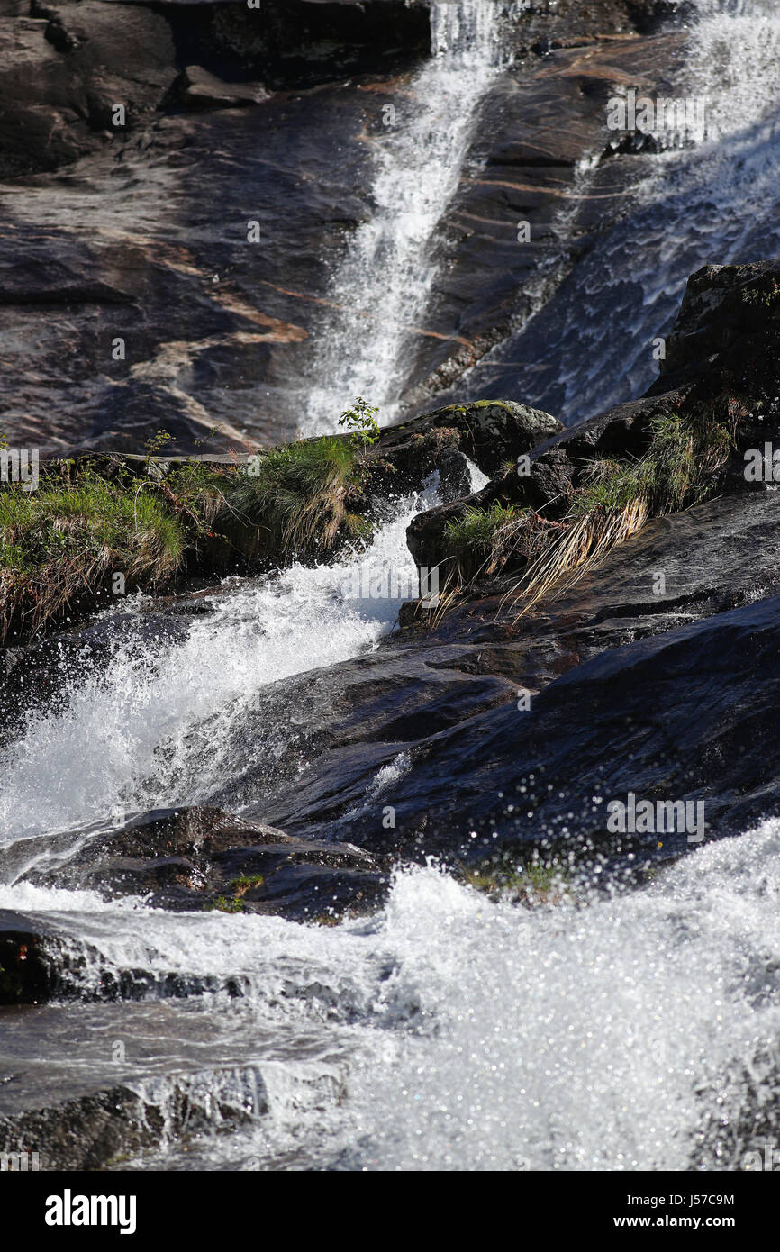 Water dripping down a tall mountain waterfall with lush vegetation ...