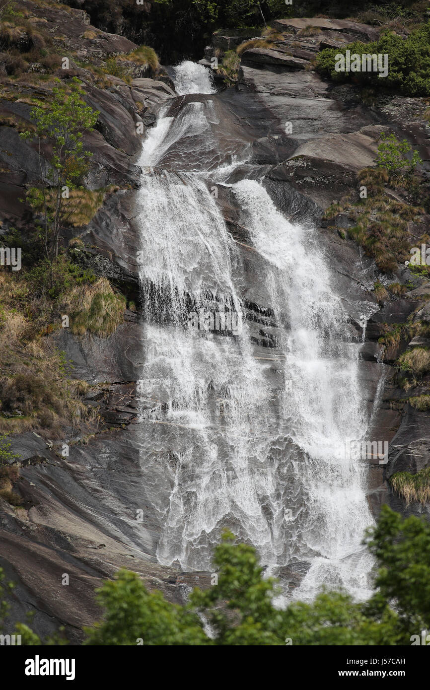 Water dripping down a tall mountain waterfall with lush vegetation ...