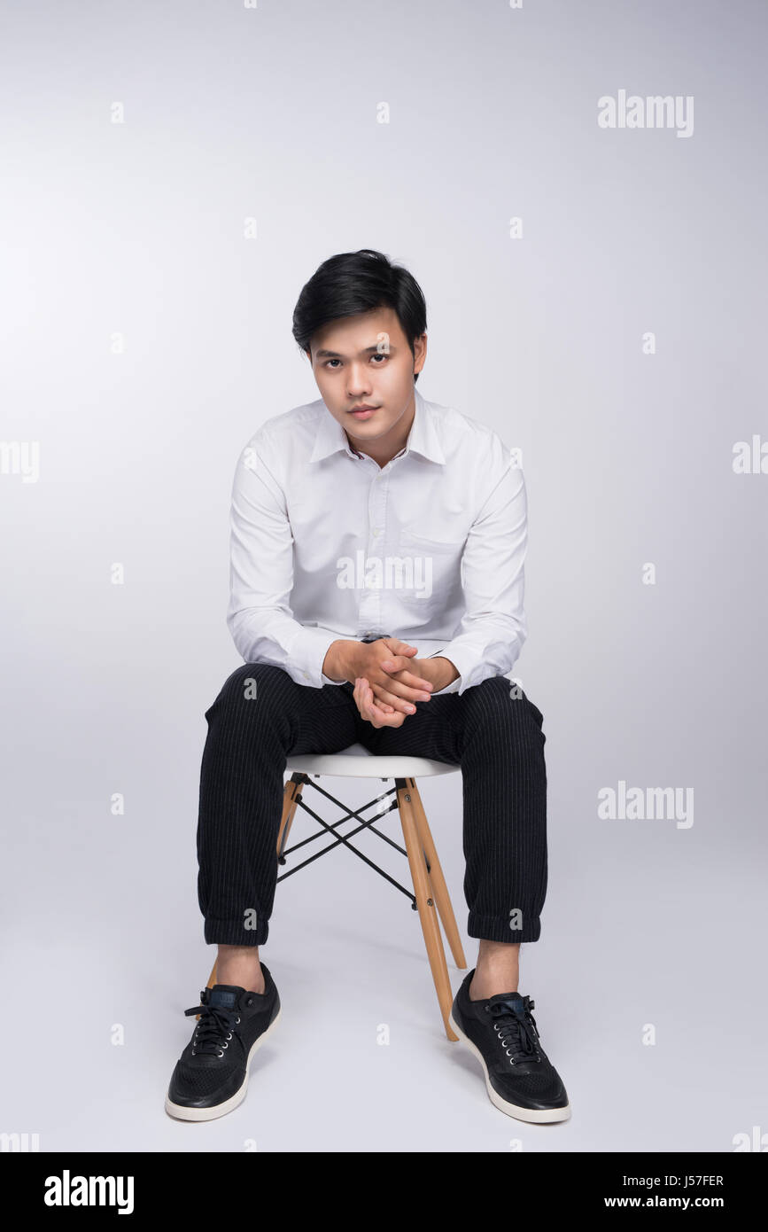 Smart casual asian man seated on chair, posing while looking at camera ...