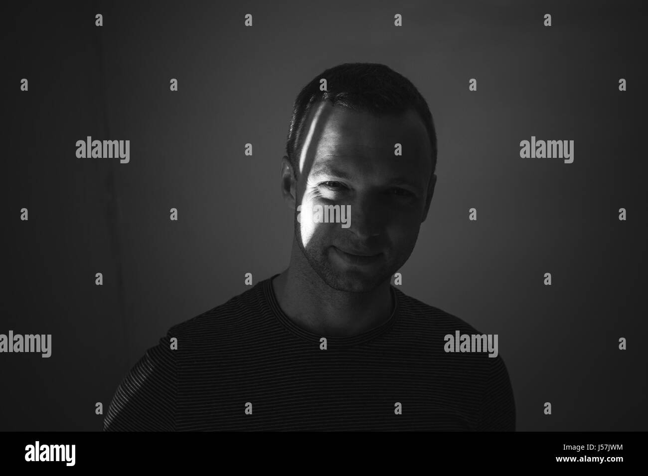 Dark artistic studio portrait of young adult European man sitting in ...