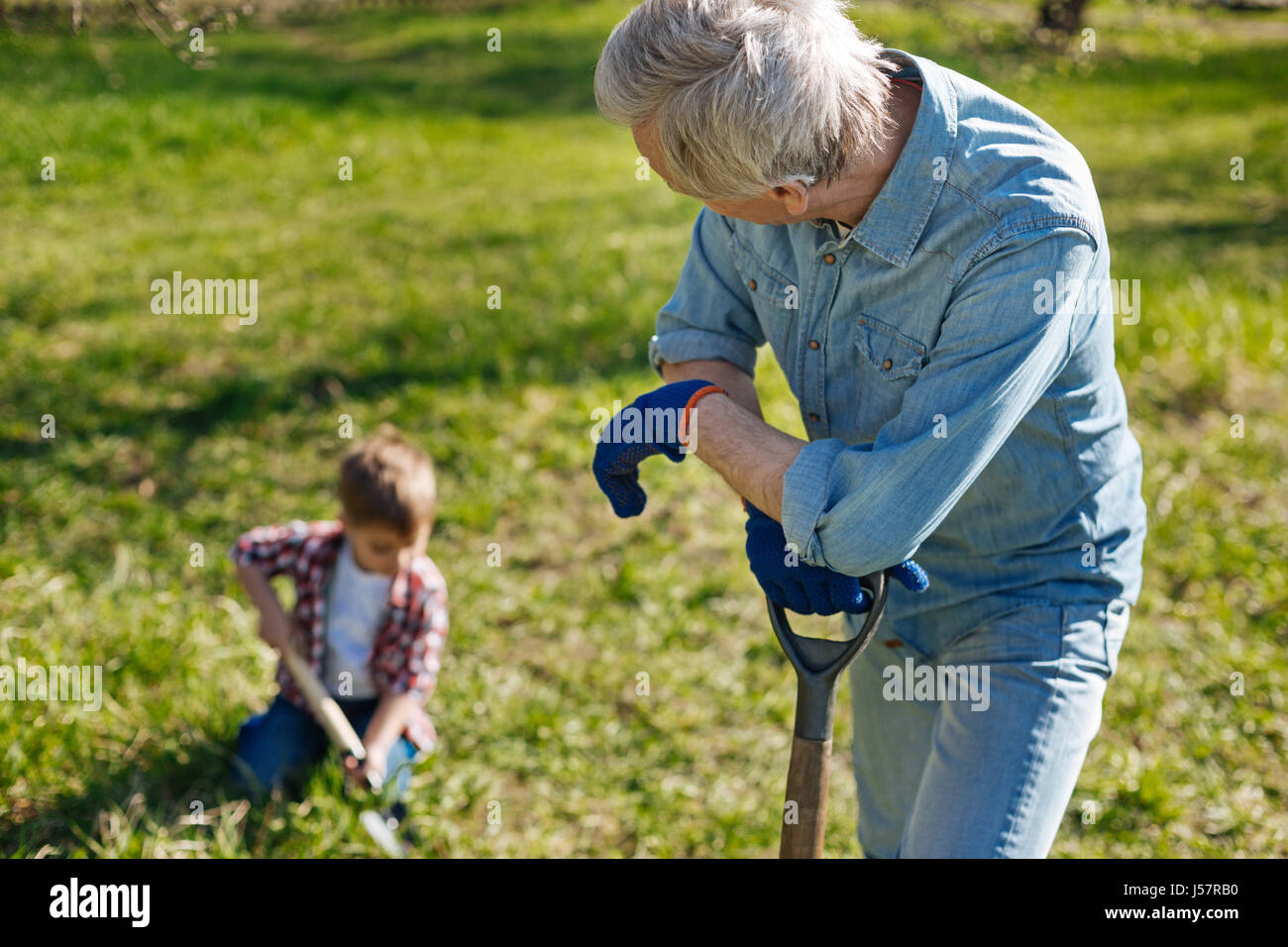Grandfather looking at child scooping ground Stock Photo - Alamy
