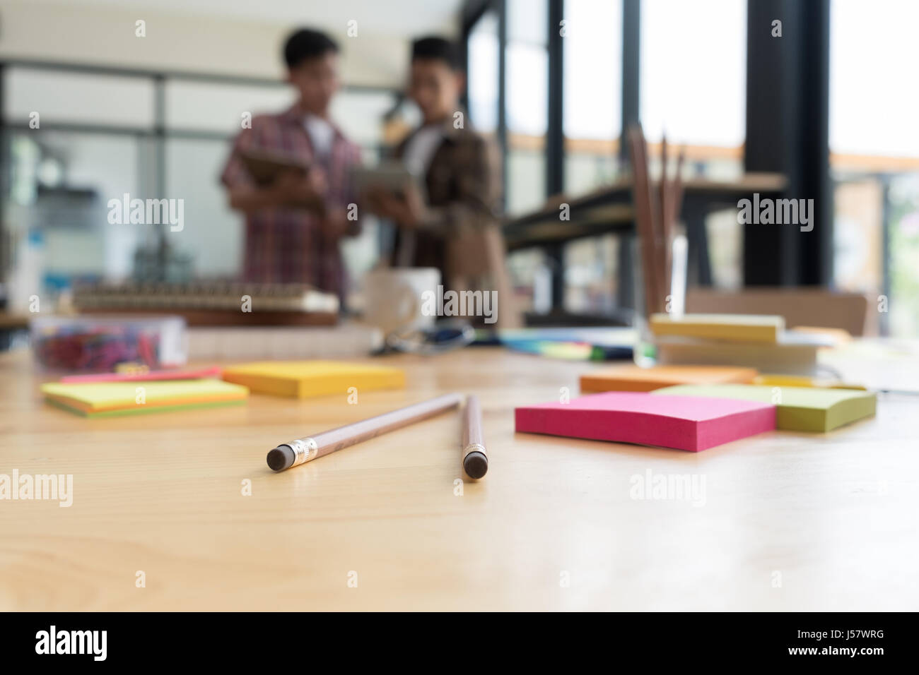 pencil and sticky note on table with background of young university ...