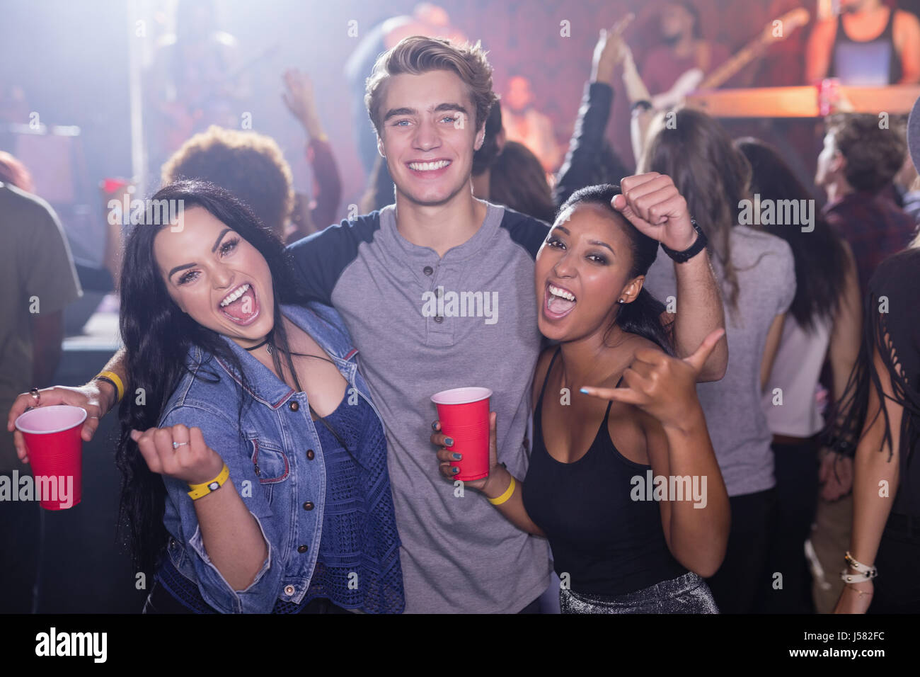Portrait of cheerful friends holding disposable cups while standing at ...