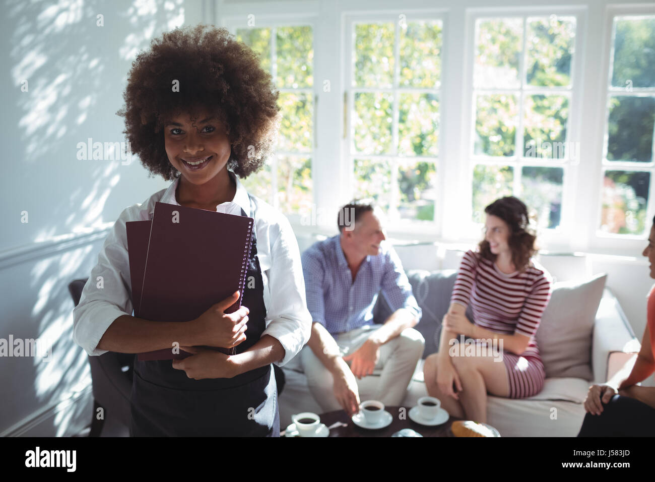 Portrait of smiling waitress standing with menu card in restaurant ...