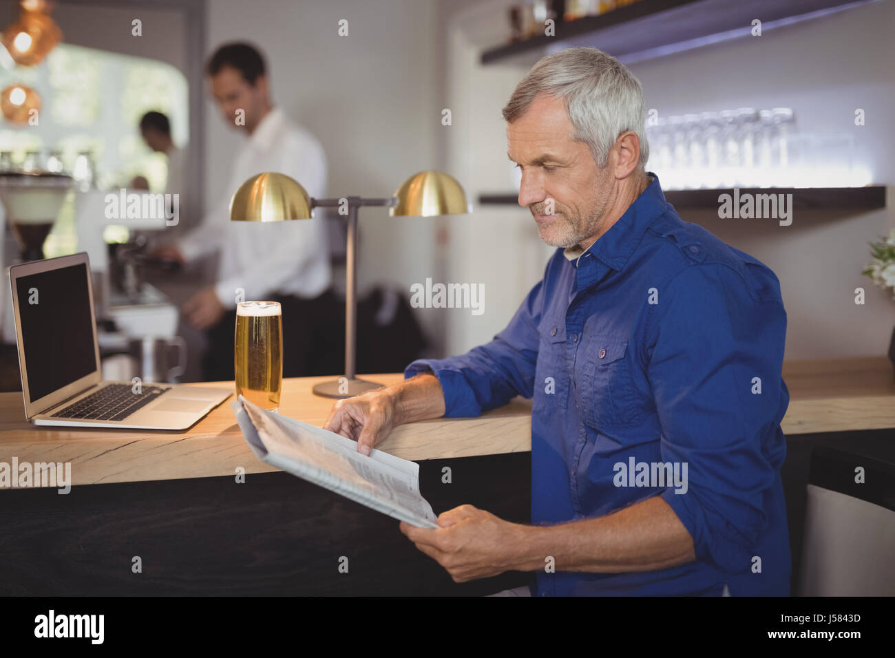 Mature man reading newspaper at counter in restaurant Stock Photo - Alamy
