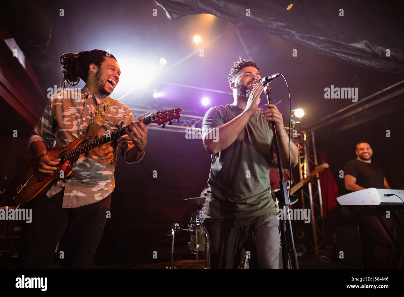 Cheerful guitarist with singer performing on stage at nightclub during ...