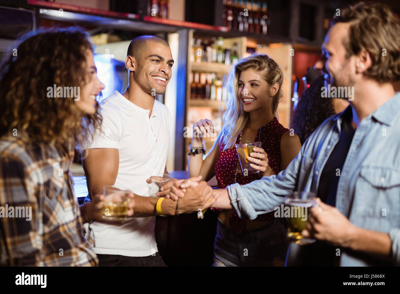 Male friends doing handshake while holding drinks by counter in counter ...