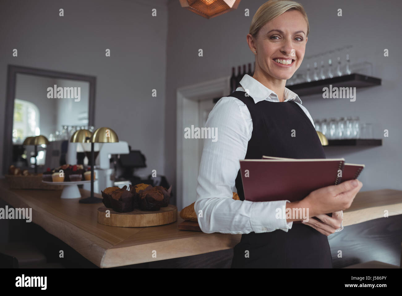 Portrait of smiling waitress standing with menu card in restaurant ...