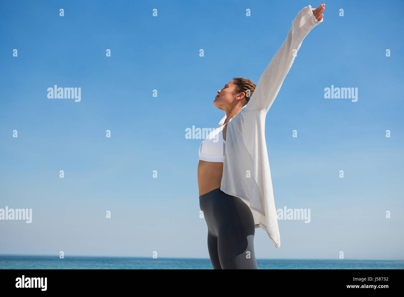 Side view of woman with arms outstretched standing at beach against sky ...