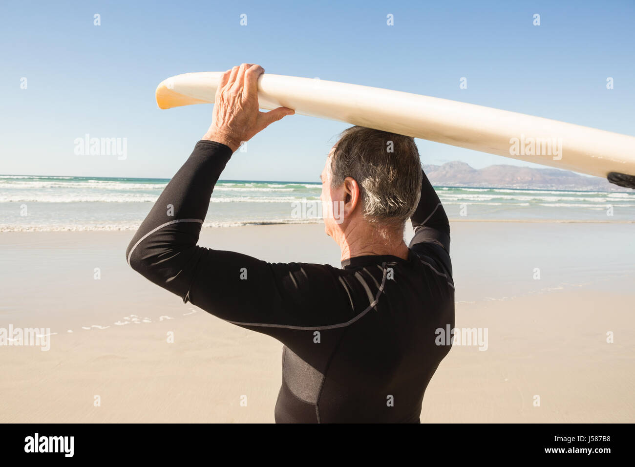 Rear view of man carrying surfboard while standing at beach Stock Photo ...