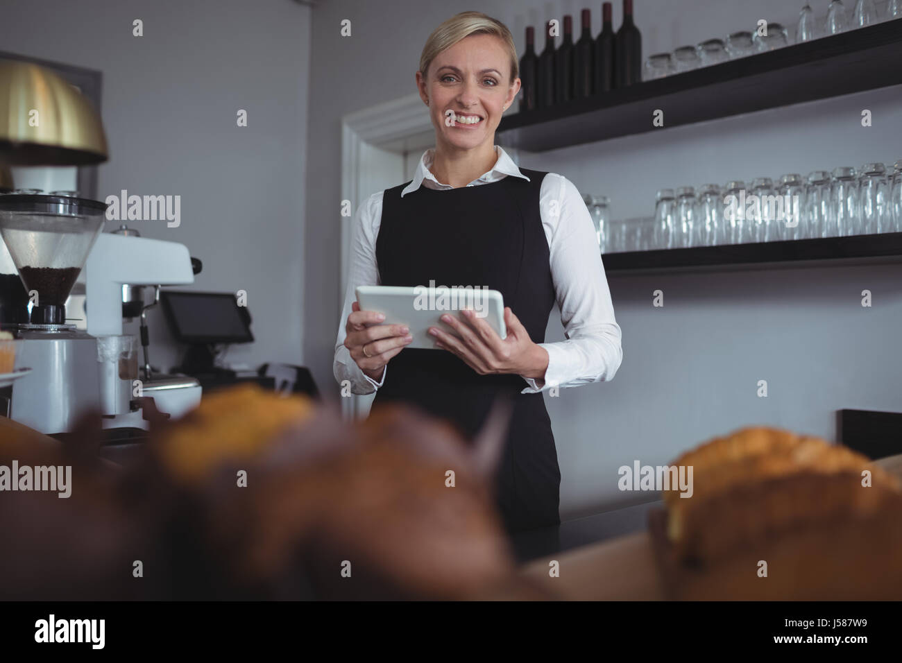 Portrait of smiling waitress holding digital tablet at counter in ...