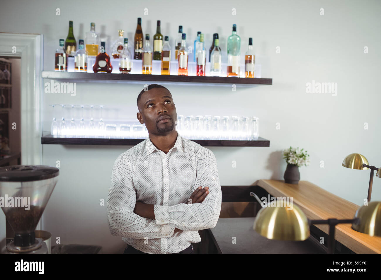 Thoughtful bar tender standing with arms crossed at bar counter in ...