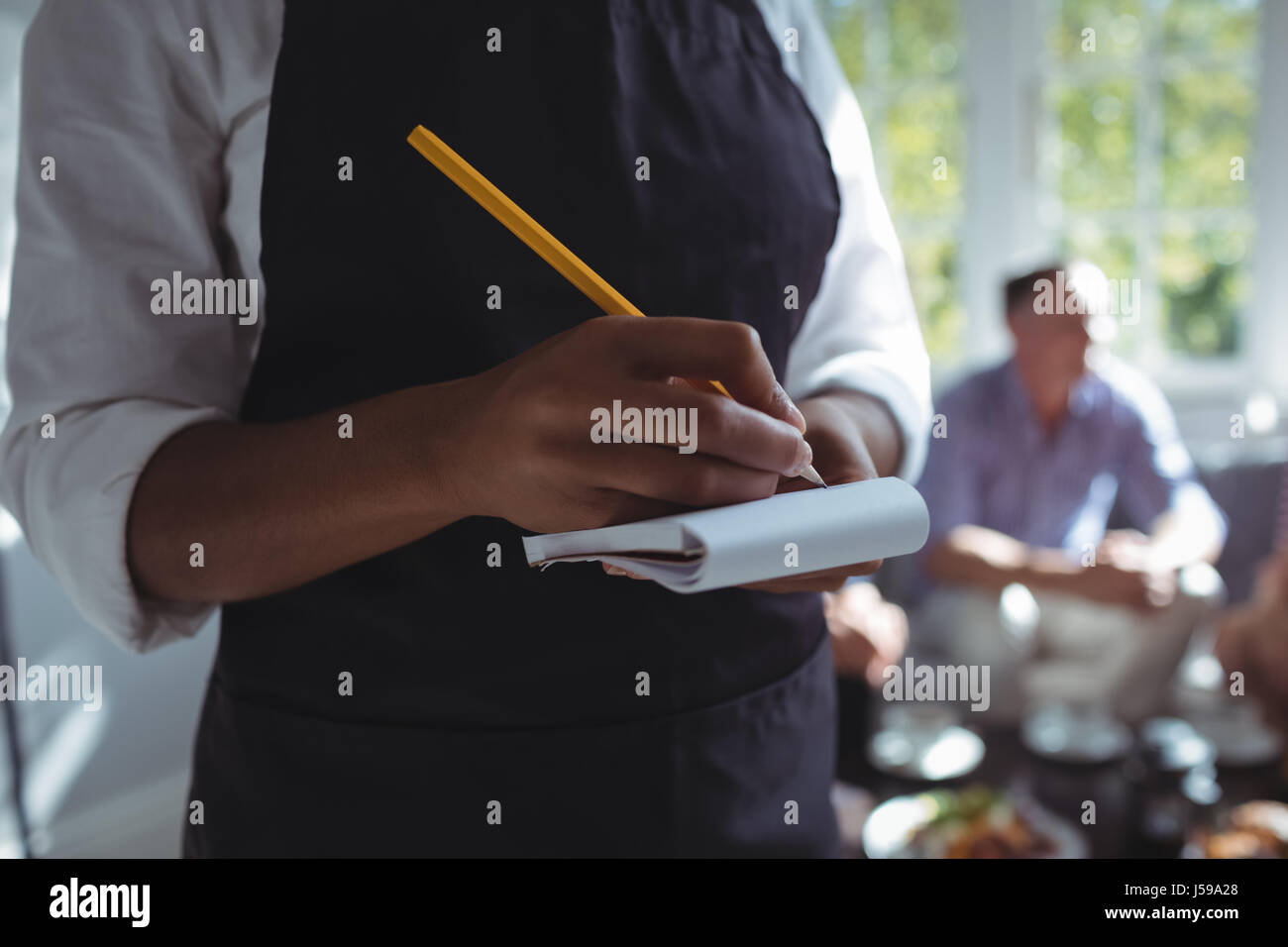 Mid section of waitress writing order on notepad while friends ...