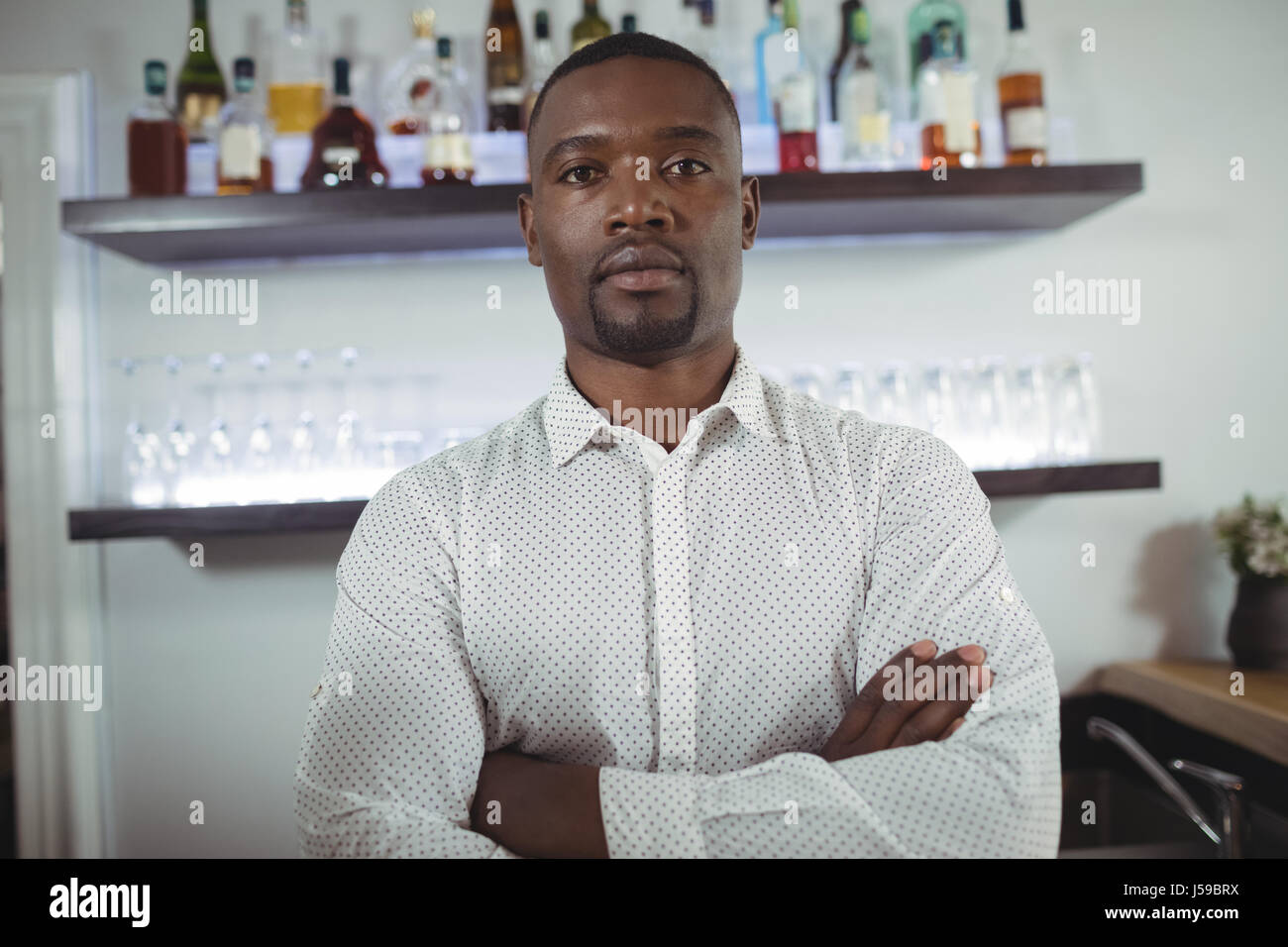 Portrait of bar tender standing with arms crossed at bar counter in ...