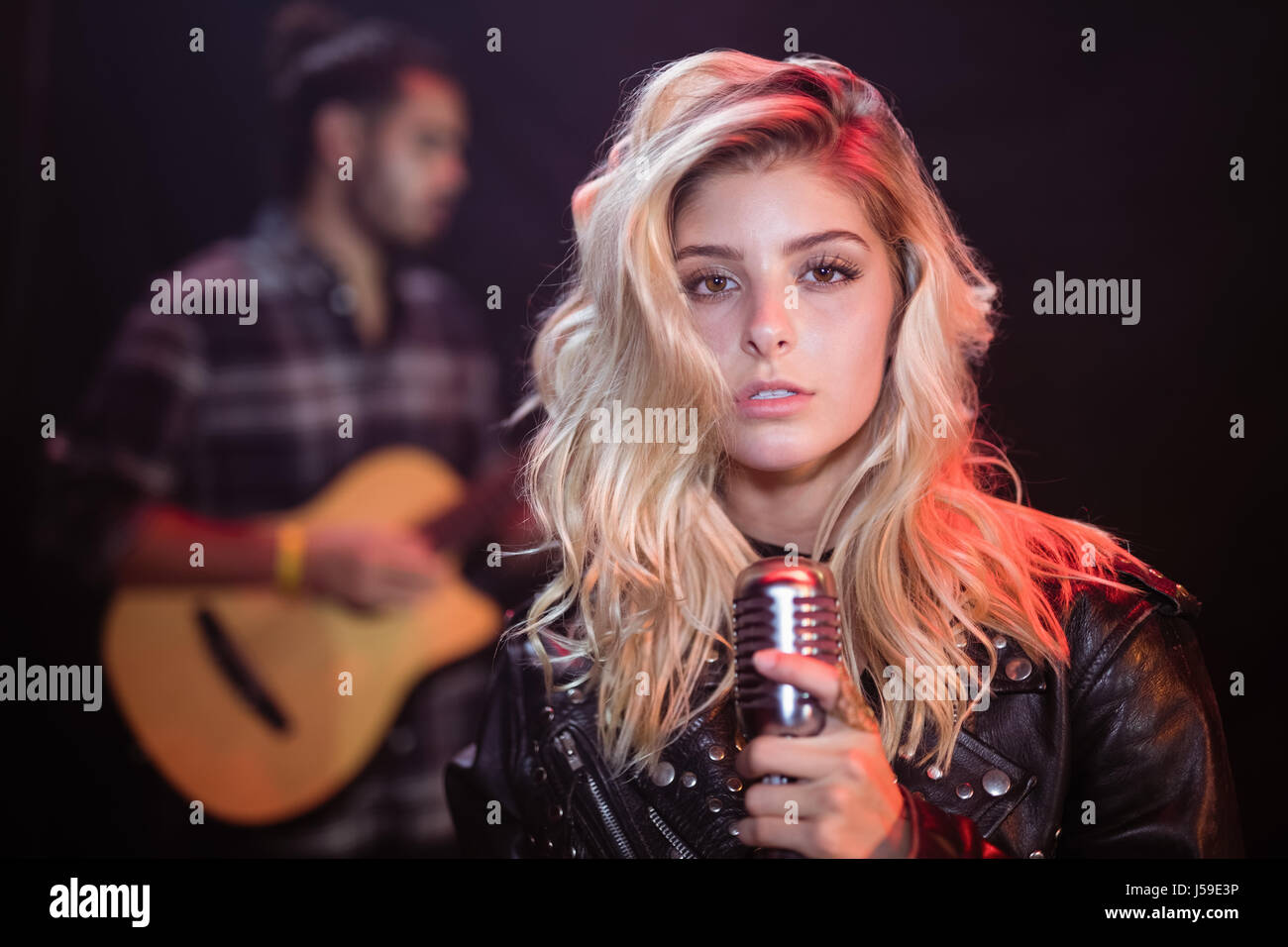 Portrait of young female singer holding mic at nightclub during music ...