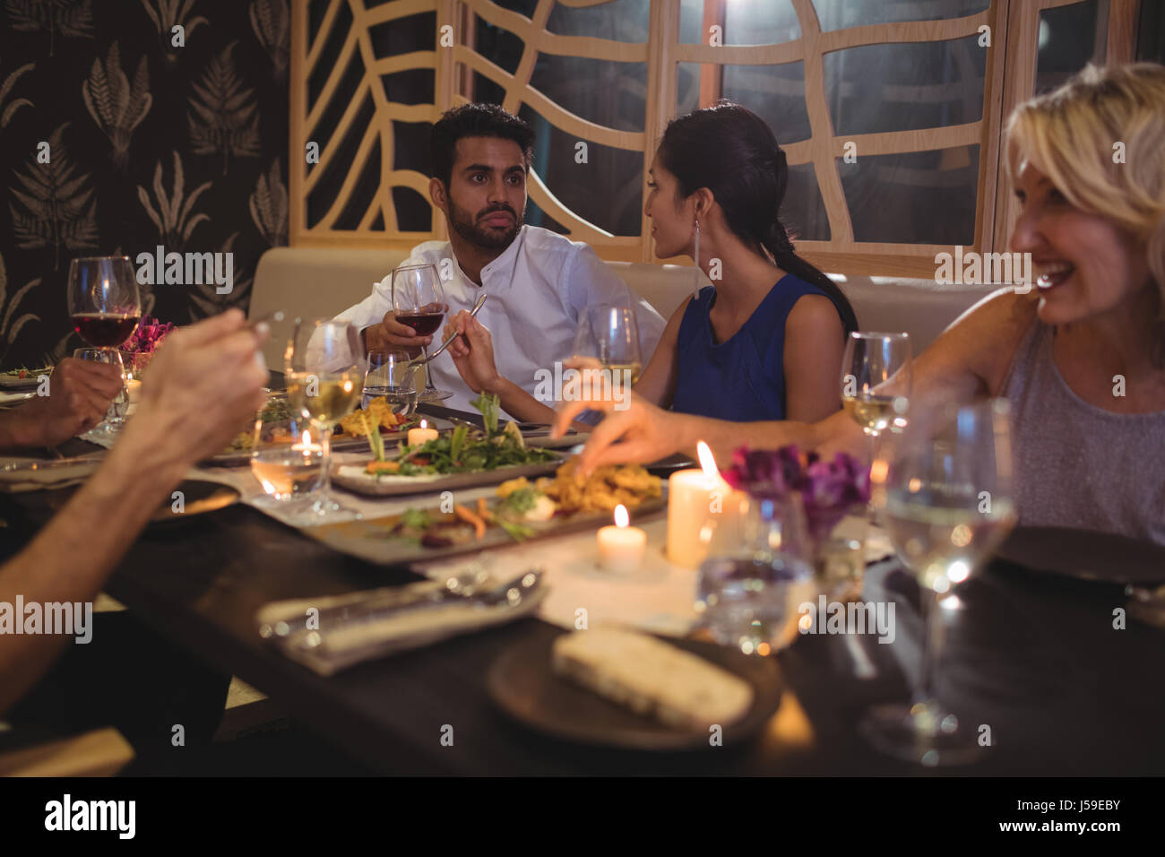 Happy friends interacting with each other while having dinner in ...