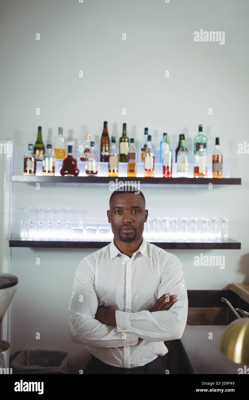 Portrait of bar tender standing with arms crossed at bar counter in ...