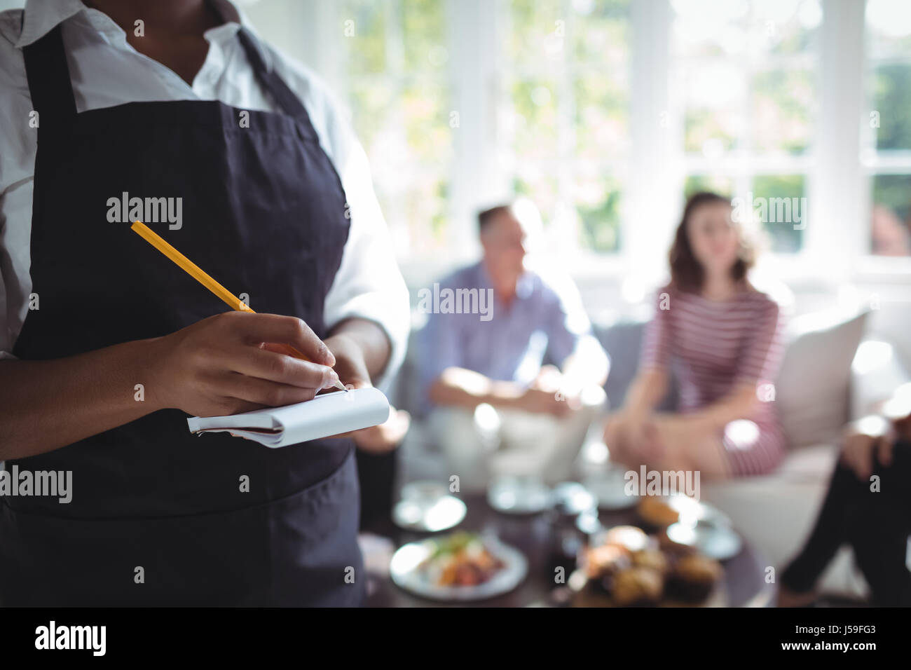 Mid section of waitress writing order on notepad while friends ...