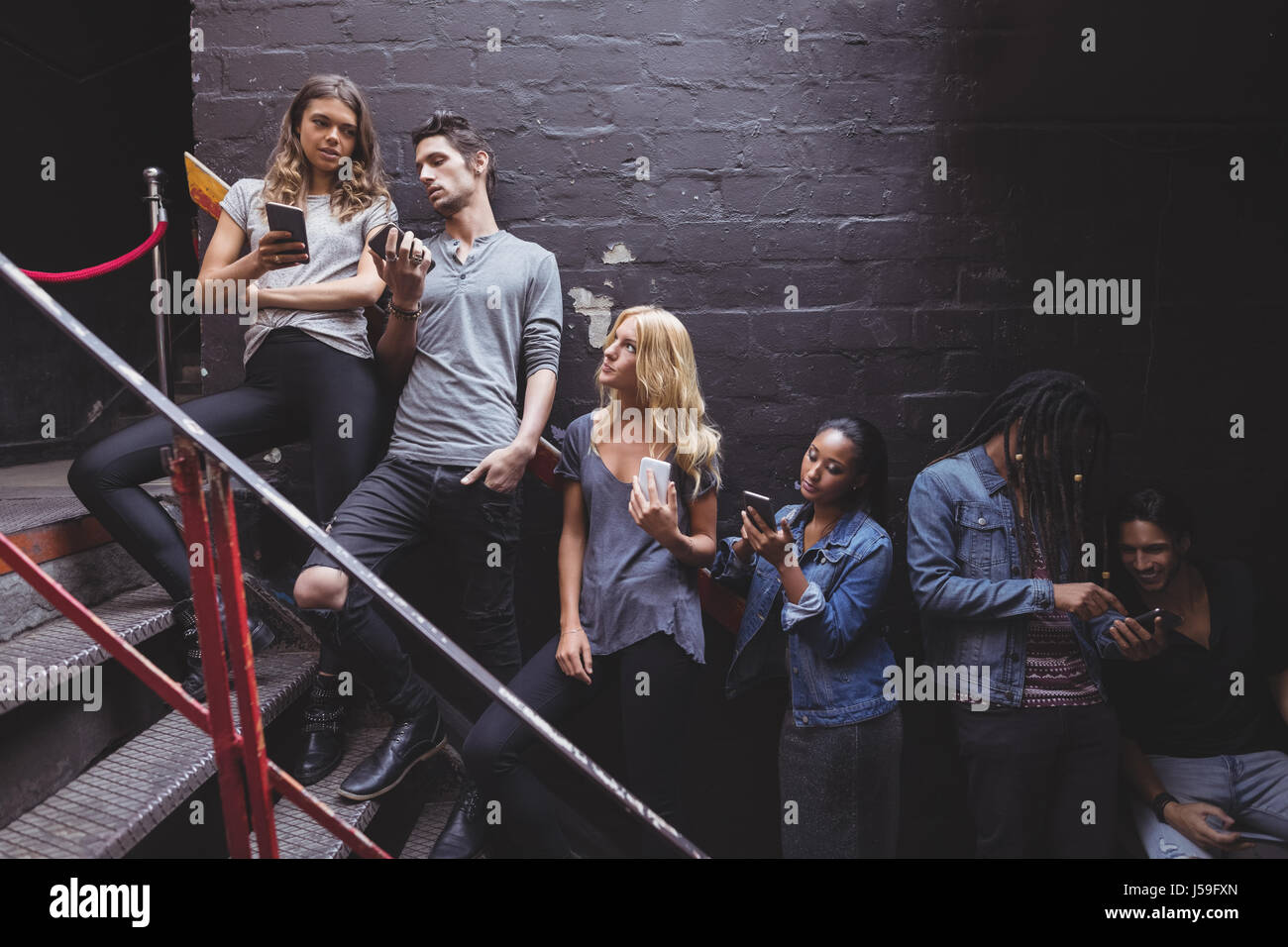 Young friends using mobile phone while waiting in line at nightclub ...