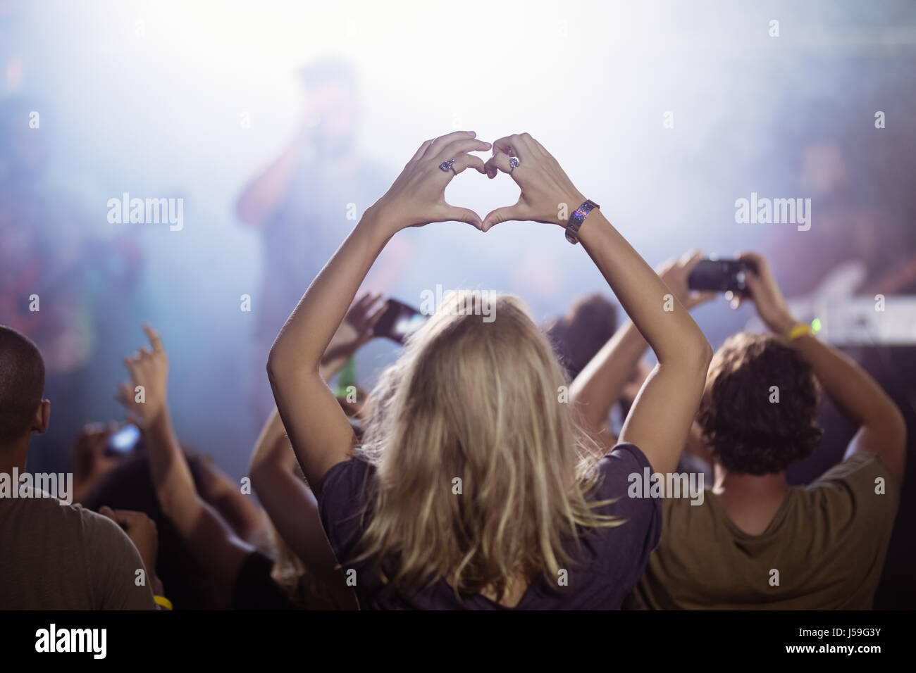 Rear view of woman making heart shape while enjoying at nightclub ...