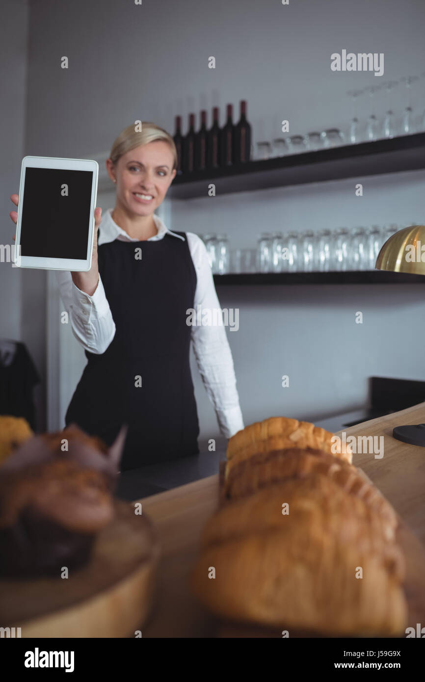 Portrait of smiling waitress holding digital tablet at counter in ...
