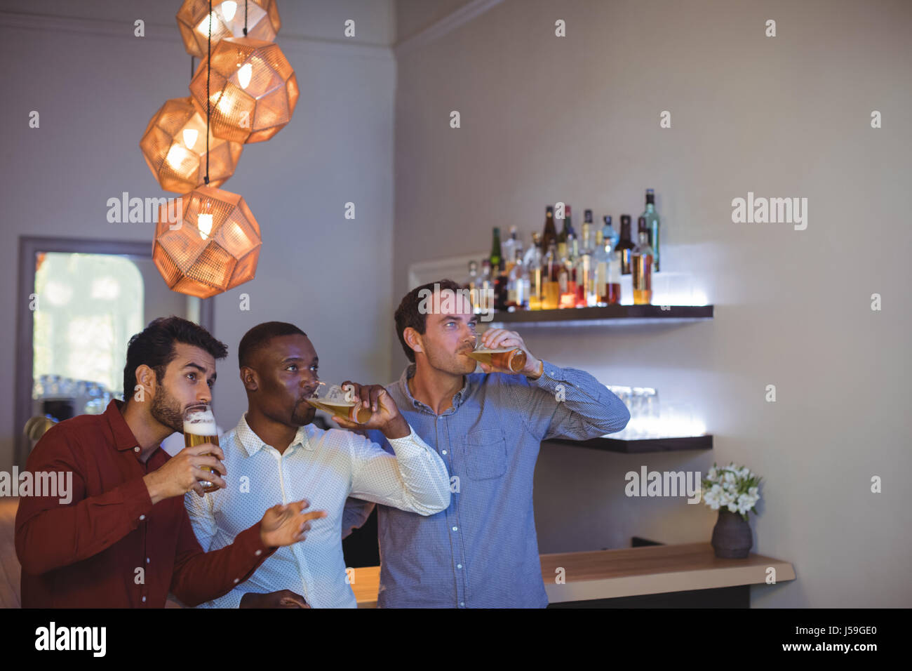 Three friends drinking beer while watching match in bar restaurant ...