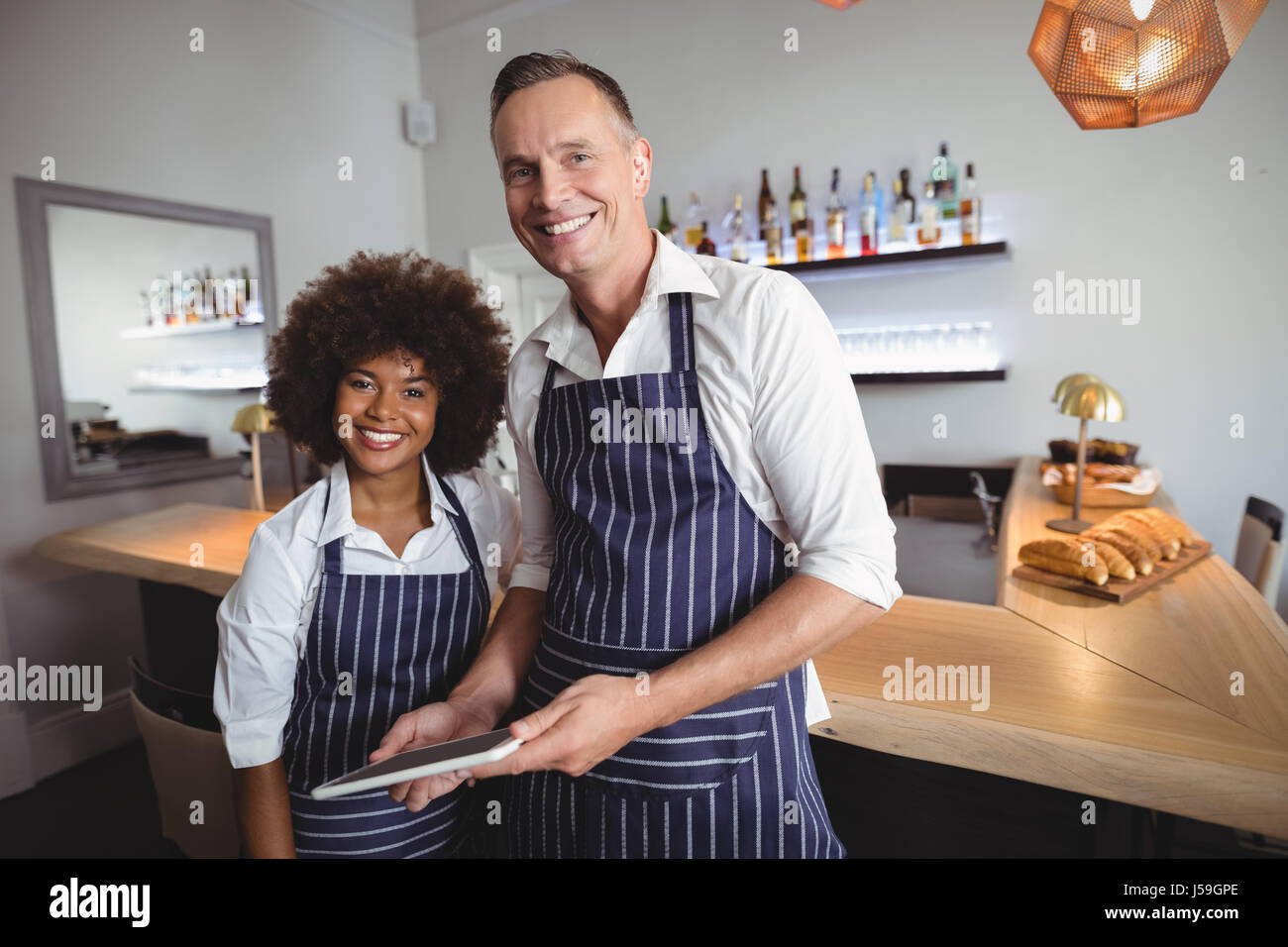 Portrait of happy waiter and waitress using digital tablet at counter ...