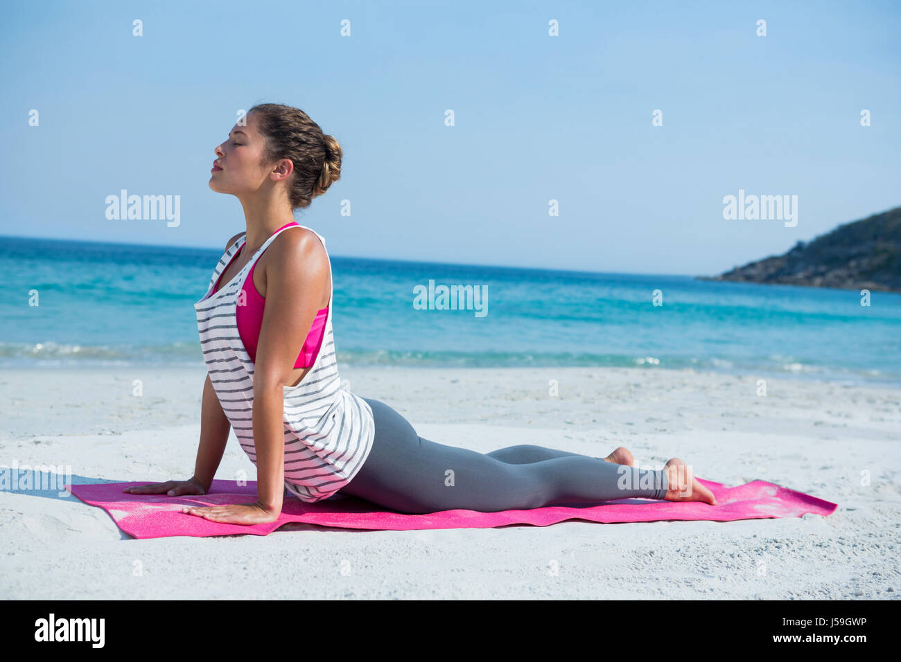 Full length of young woman practicing cobra pose at beach on sunny day ...