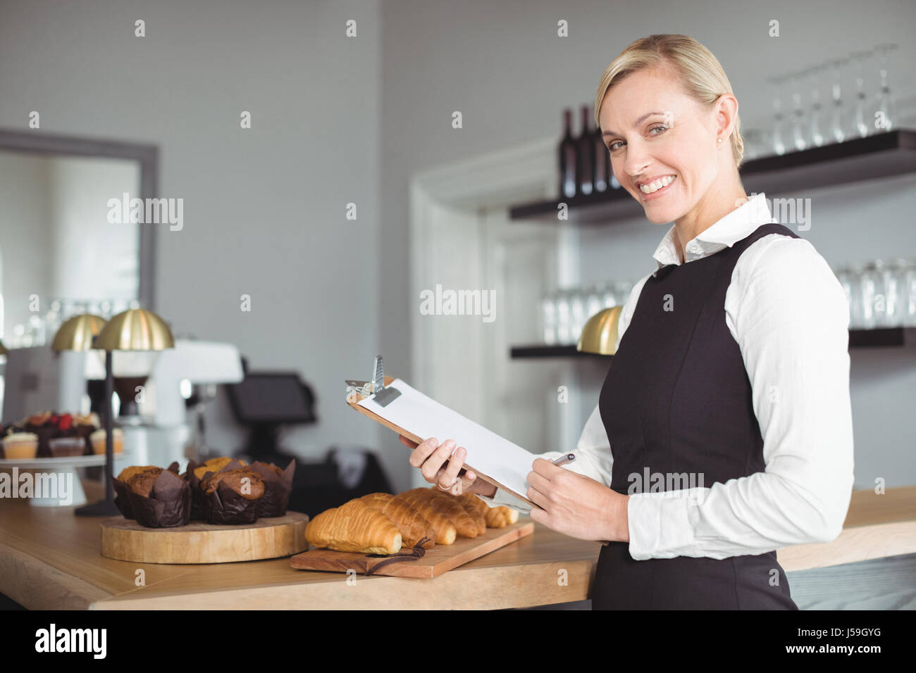 Portrait of smiling waitress with clipboard standing at counter in ...