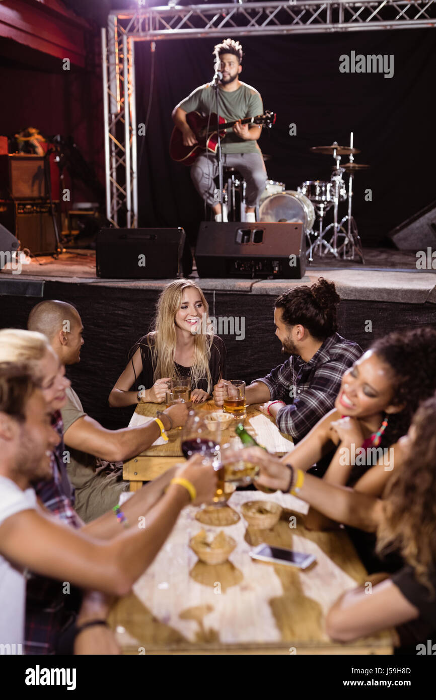 Male musician singing on stage with fans sitting at table in nightclub ...