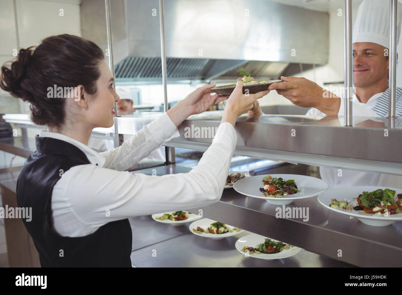 Chef handing food dish to waitress at order station in the commercial ...