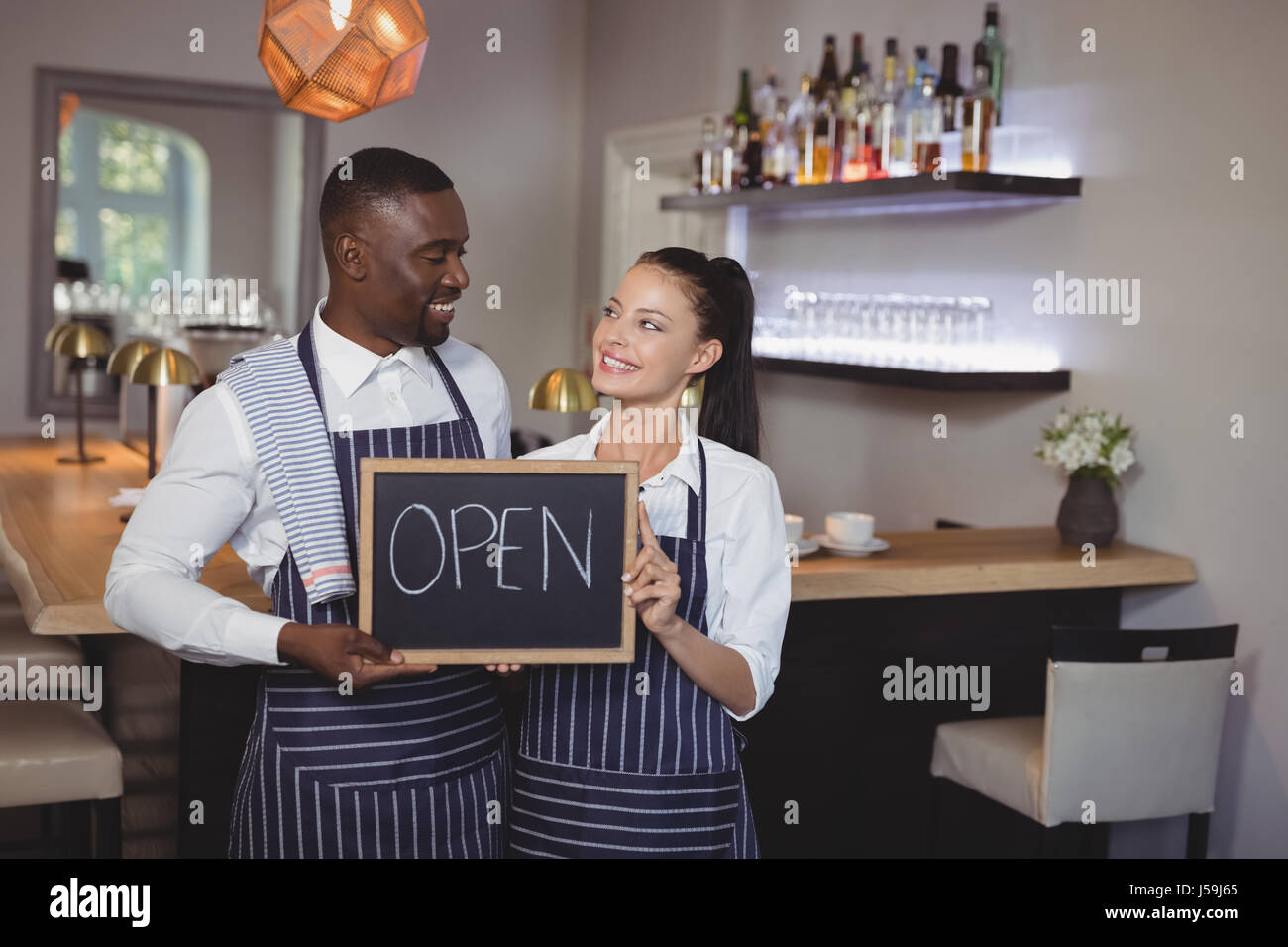Waiter and waitress showing chalkboard with open sign at counter in ...