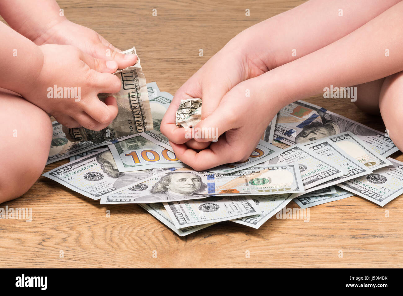 Children sit near a pile of money on a wooden board and crumple bills ...