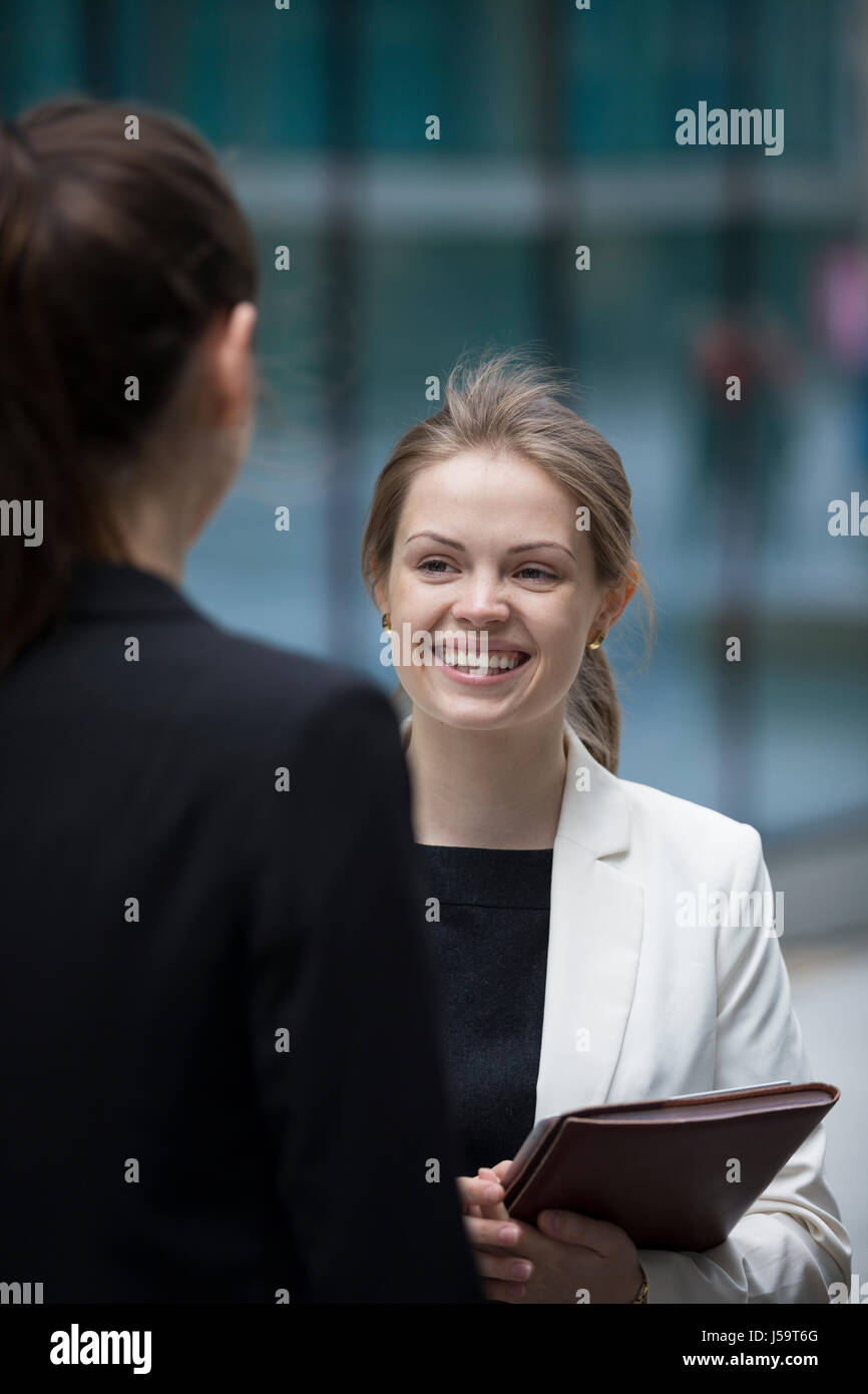 Portrait of two caucasian business women talking outside modern office ...