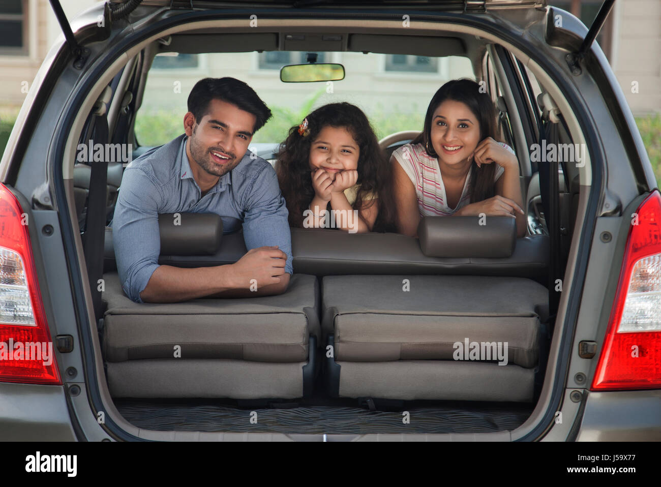Portrait of young family leaning on back seat with open boot of car ...