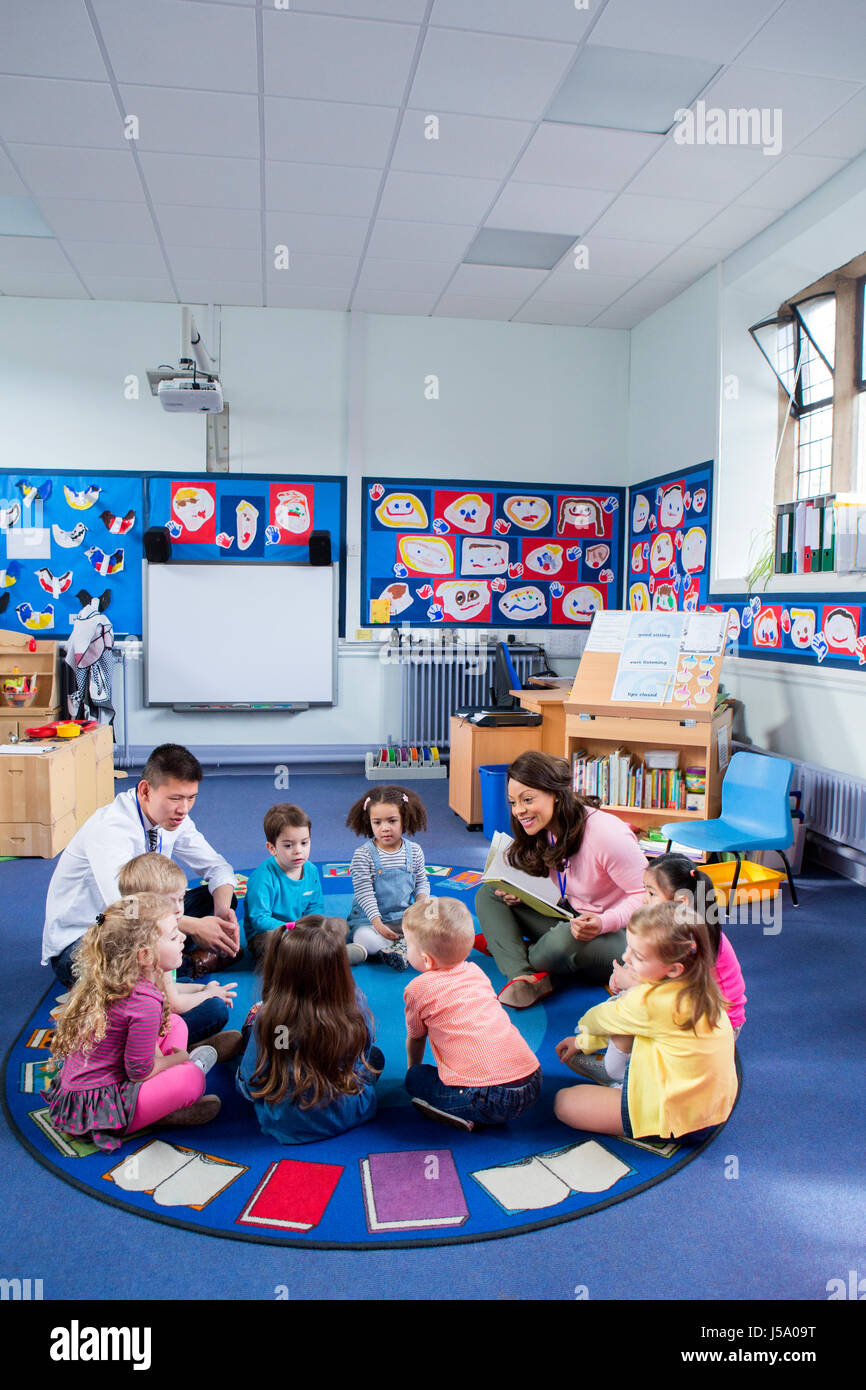 Group of nursery children sitting on the floor in their classroom with ...