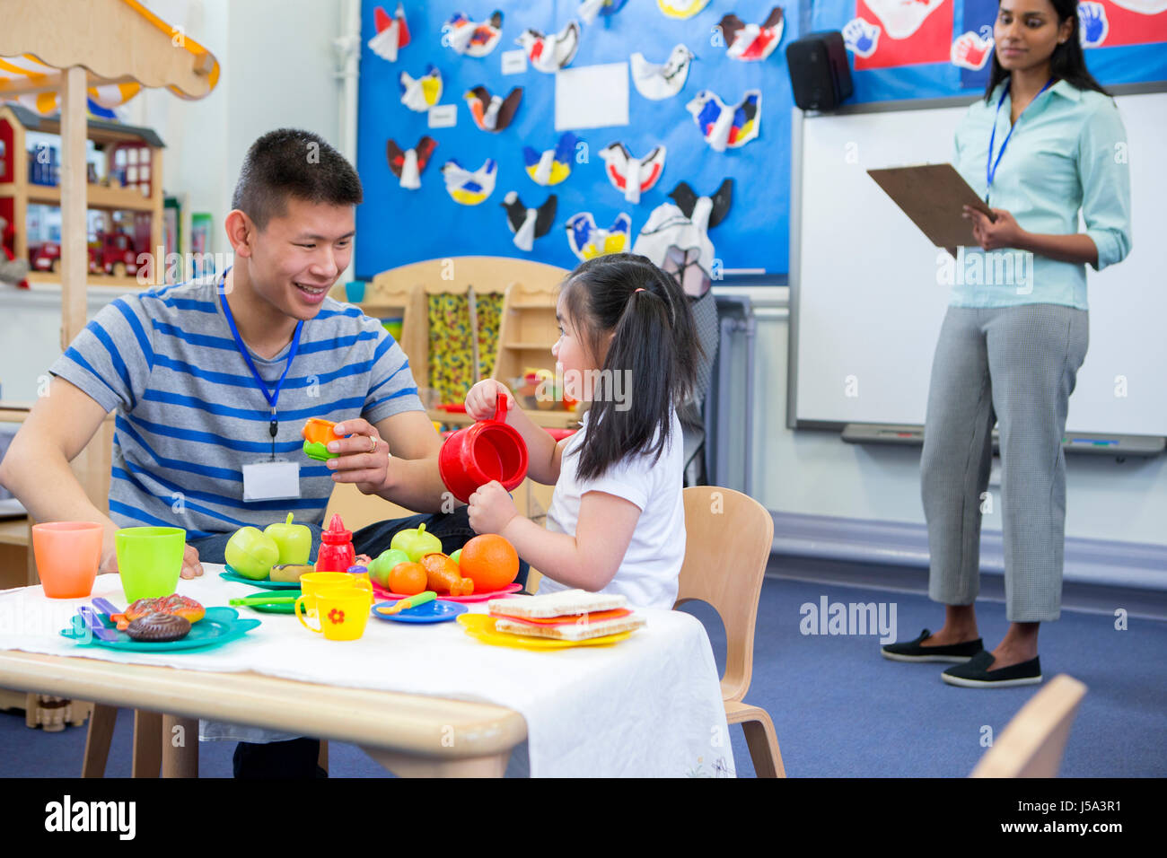 Male teacher playing in a toy kitchen with a nursery student. There is ...