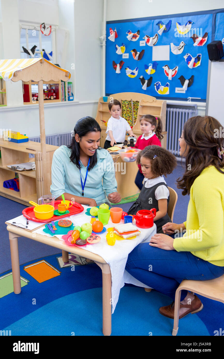 Teachers playing with plastic kitchen toys with their nursery students ...