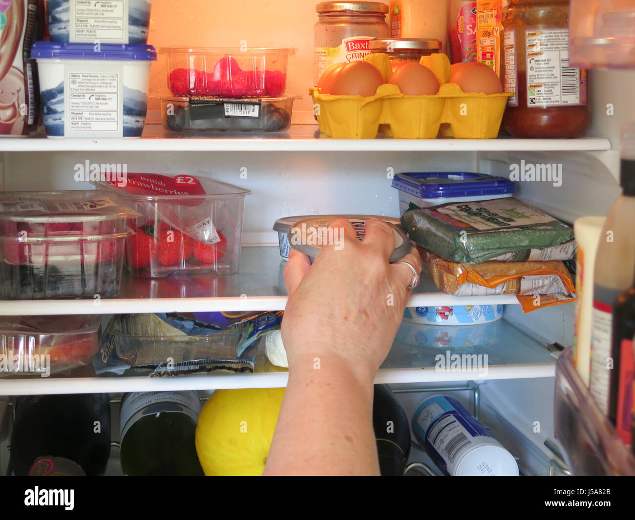 Food inside fridge with hand reaching Stock Photo - Alamy