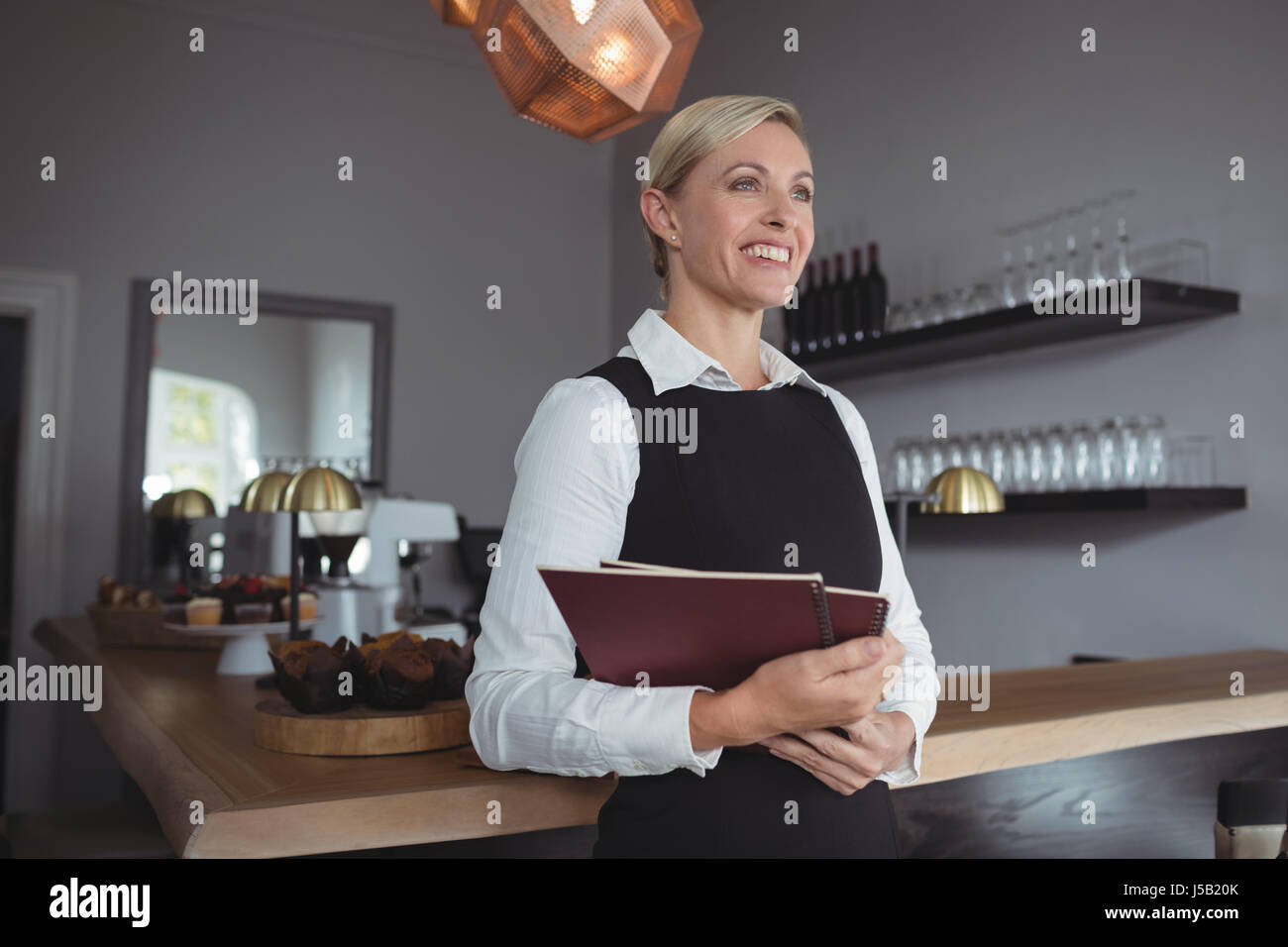 Thoughtful waitress standing with menu card in restaurant Stock Photo ...