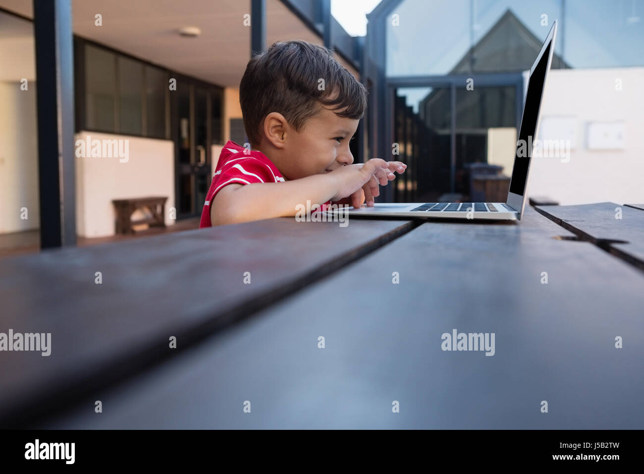 Side view of happy boy using digital laptop while sitting at table in ...