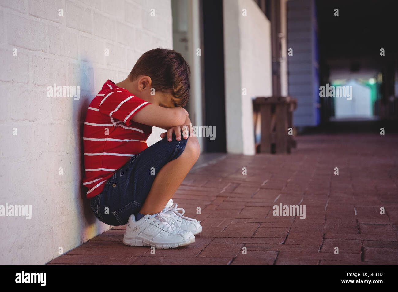 Side view of depressed boy crouching by wall at school building Stock ...