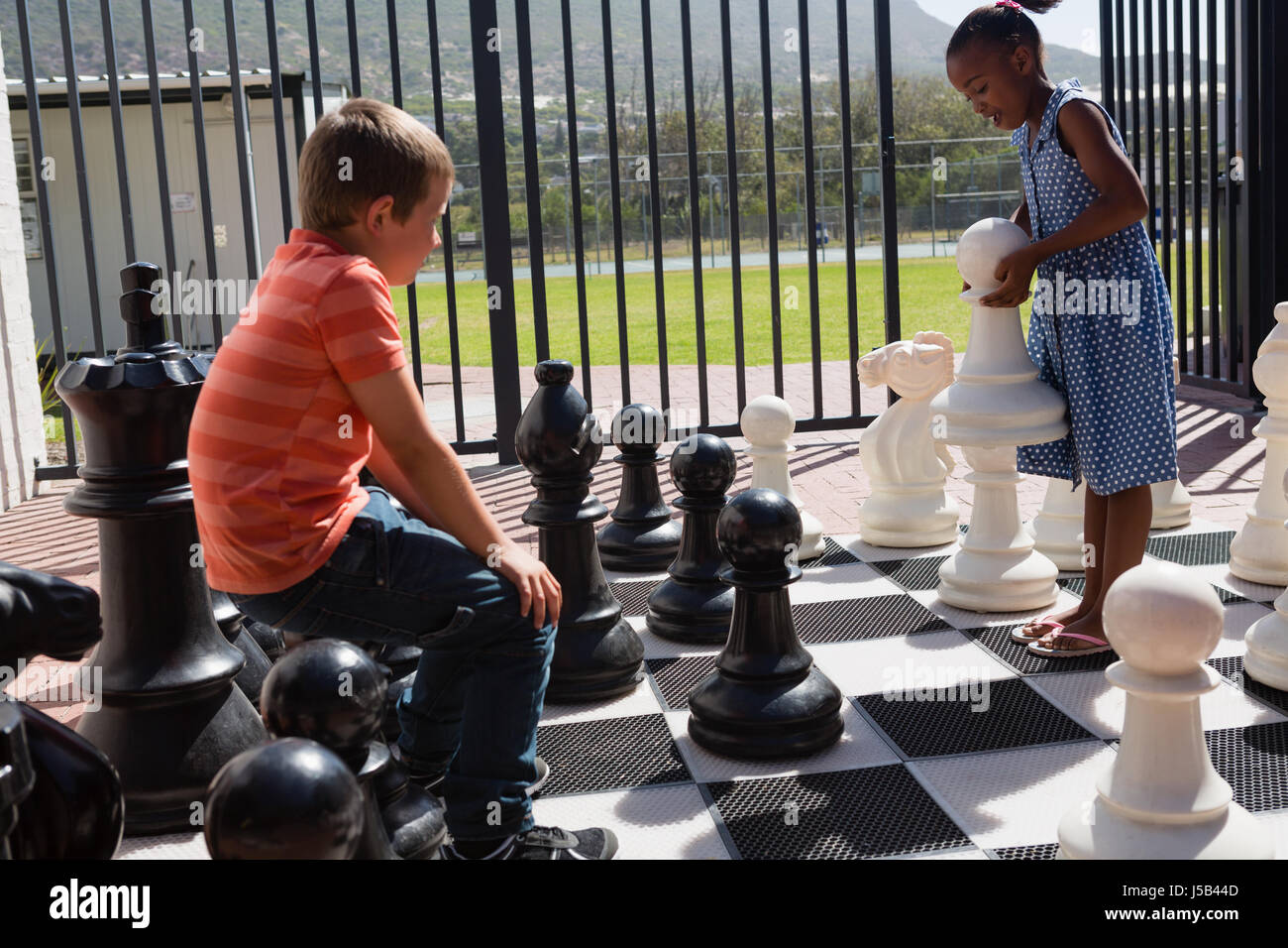Classmates playing together with large chess at school on sunny day ...