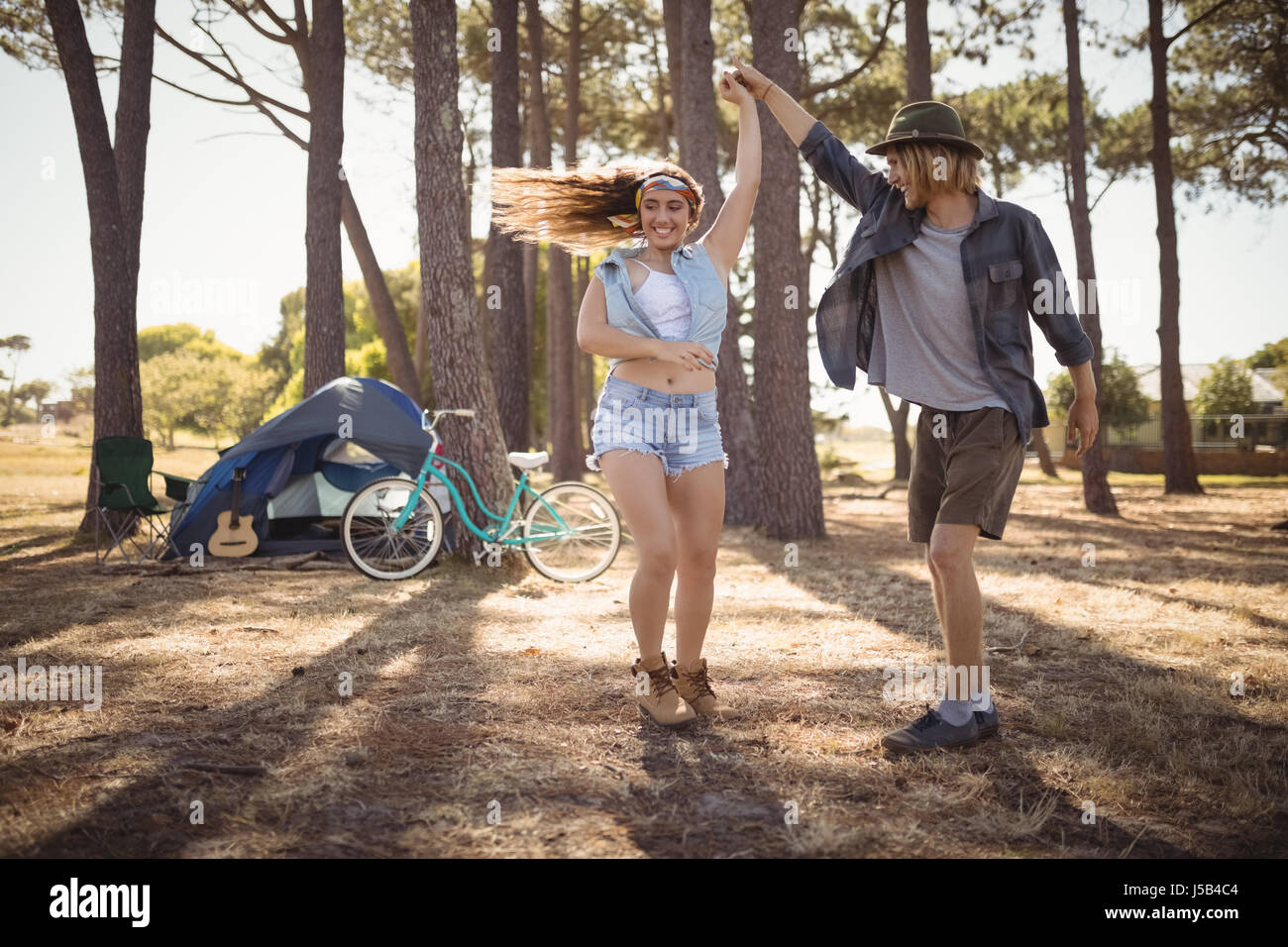 Cheerful couple dancing on field while camping at forest Stock Photo ...