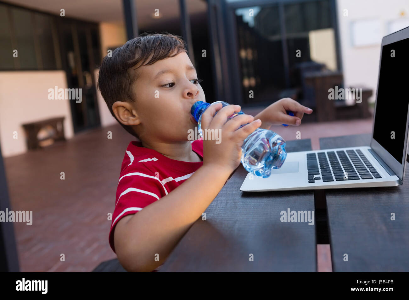 Boy drinking water while using laptop at table in school Stock Photo ...