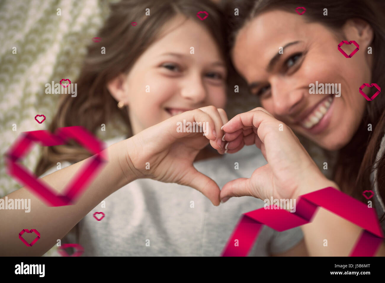 Hearts against mother and daughter making heart shape with hands while ...