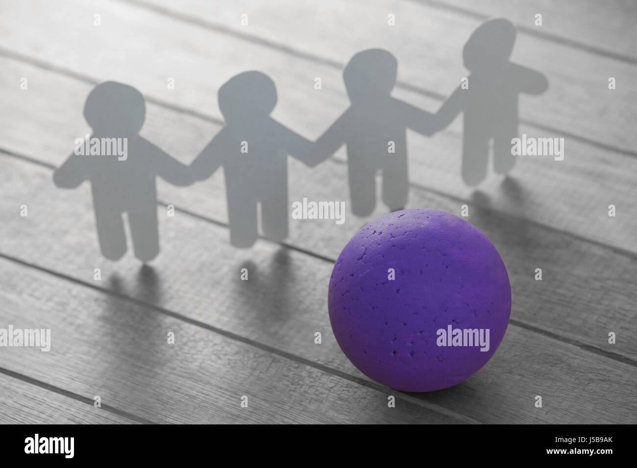 High angle view of paper cut out human chain by ball on wooden table ...