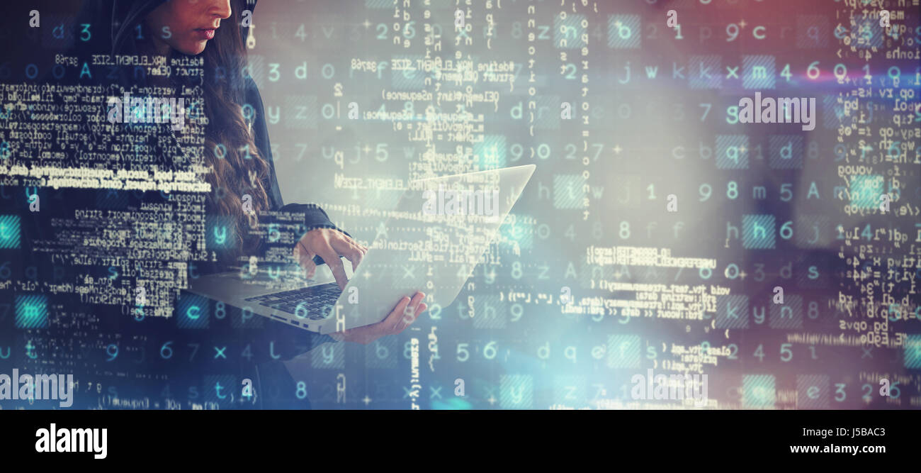 Serious female hacker using laptop while standing against white tile ...